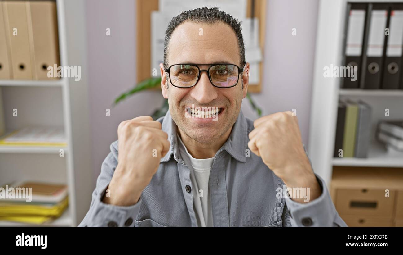 A cheerful man celebrates with fists clenched in a modern office ...