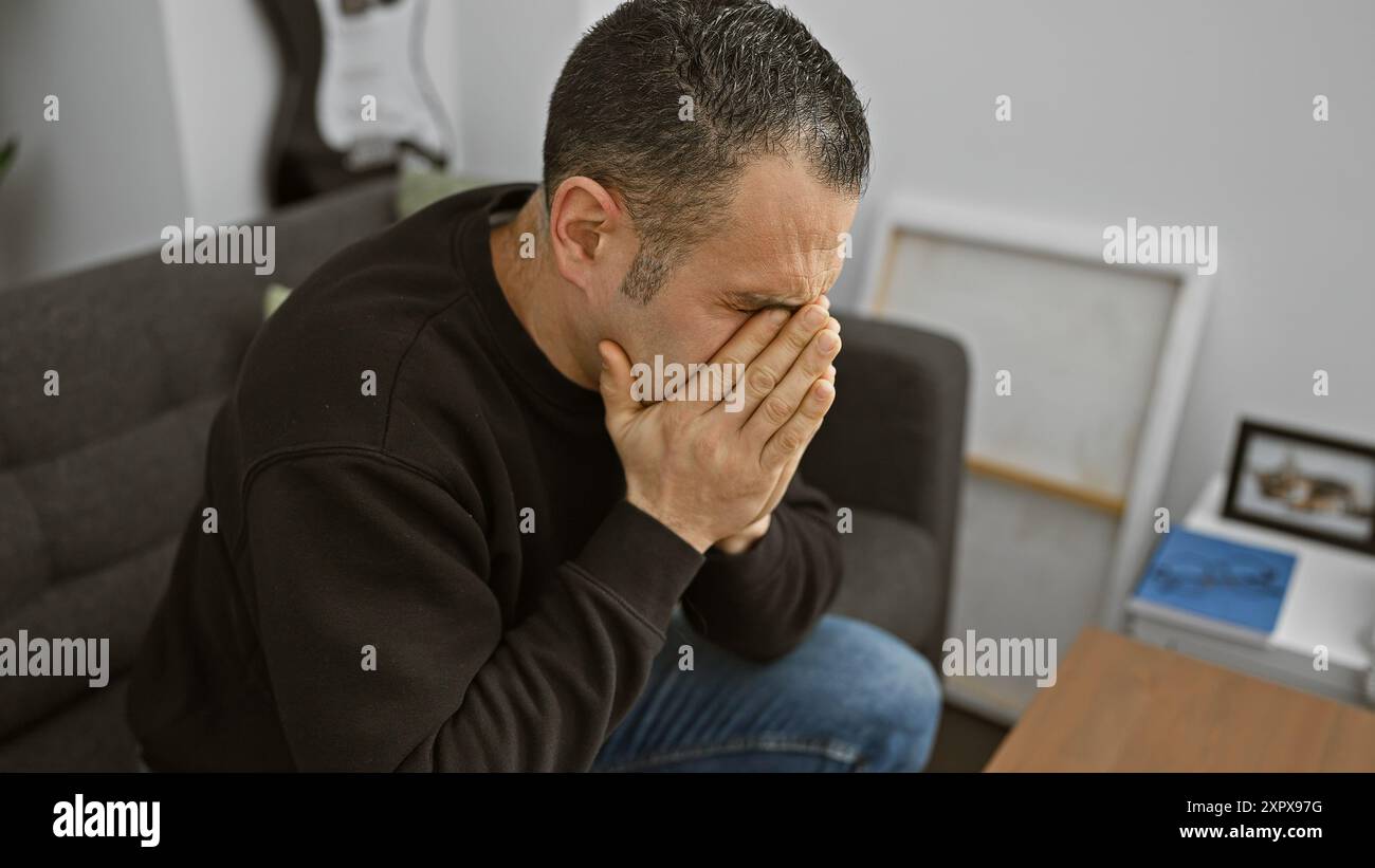 A distressed hispanic man sitting indoors with hands covering face ...