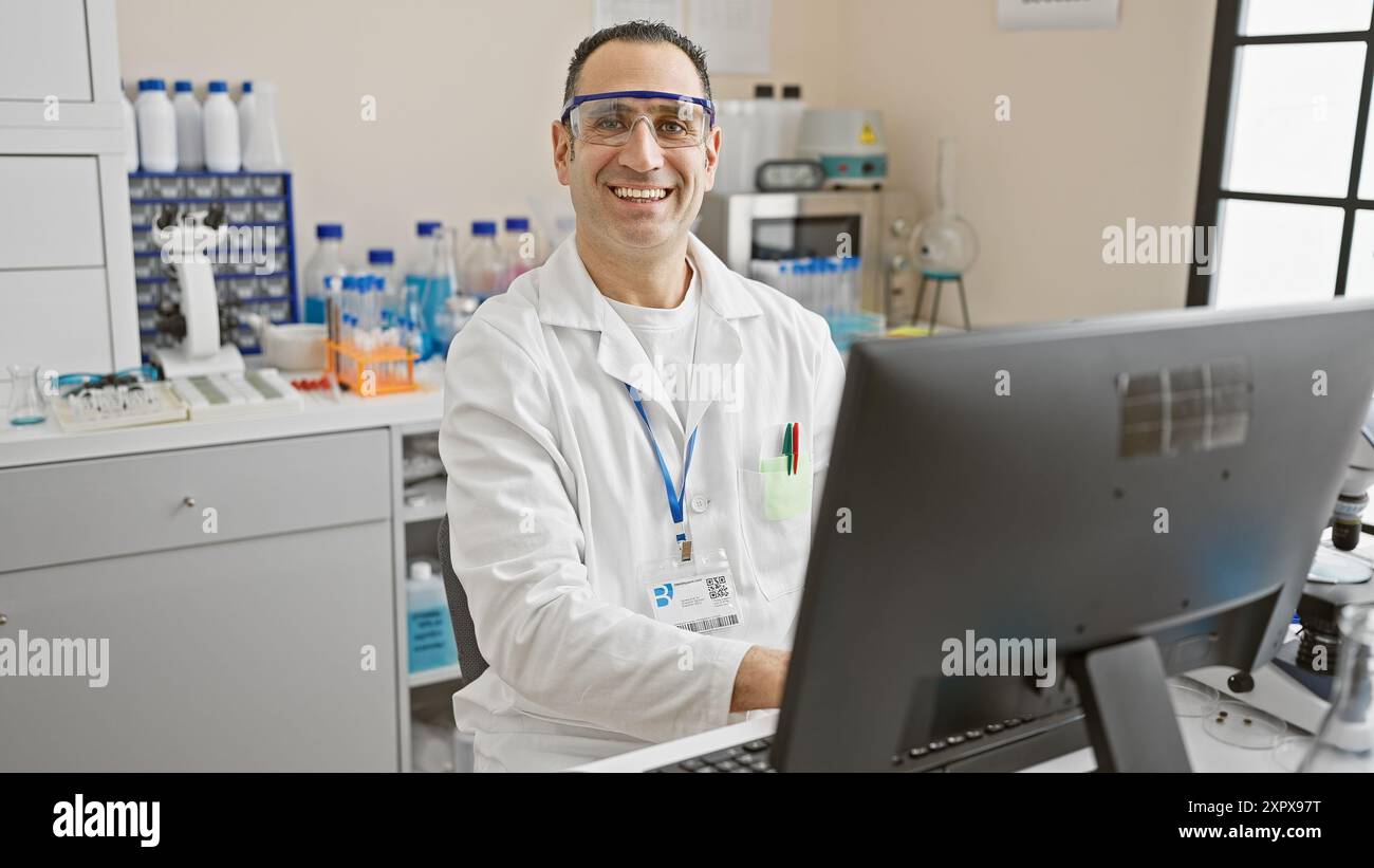 A cheerful scientist man in a lab coat works at a computer in a bright ...