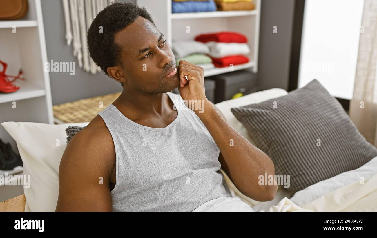 A pensive african american man sits thoughtfully on his bed in a well ...