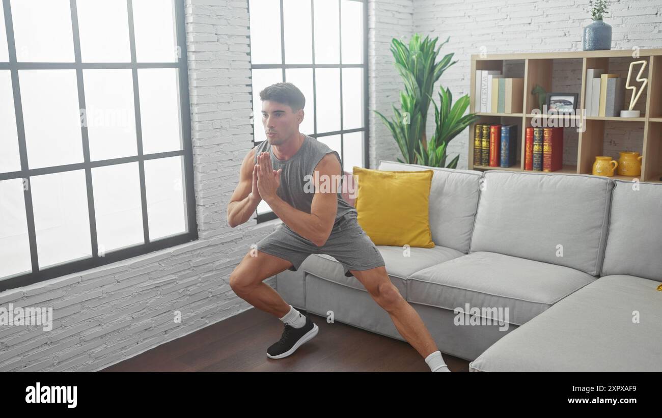 A fit man in workout clothes doing squats in a bright living room with ...