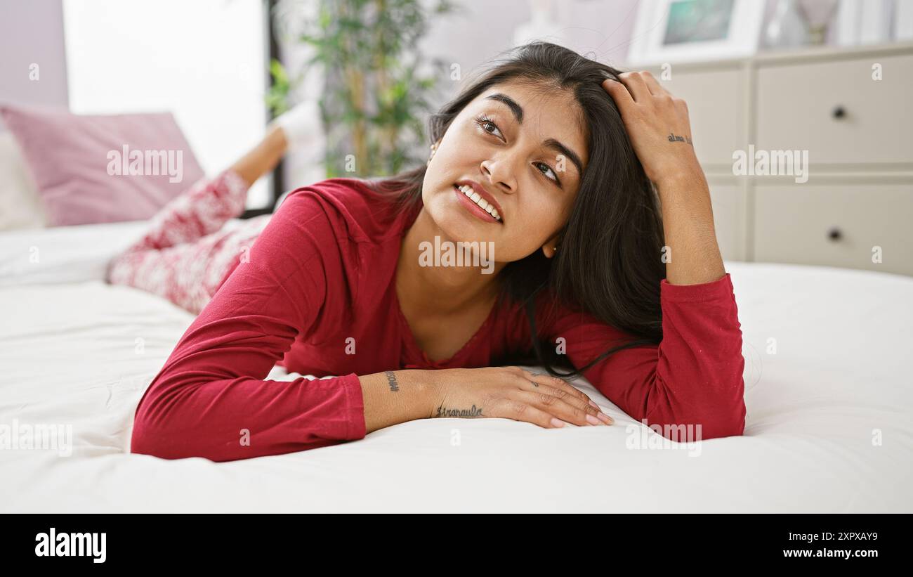 A relaxed south asian woman with long hair lounges on a bed in a cozy ...