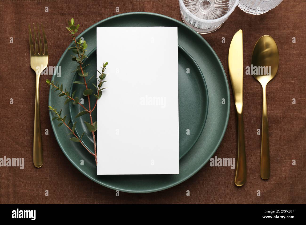 Empty menu, plates, cutlery, glass and floral decor on brown tablecloth ...