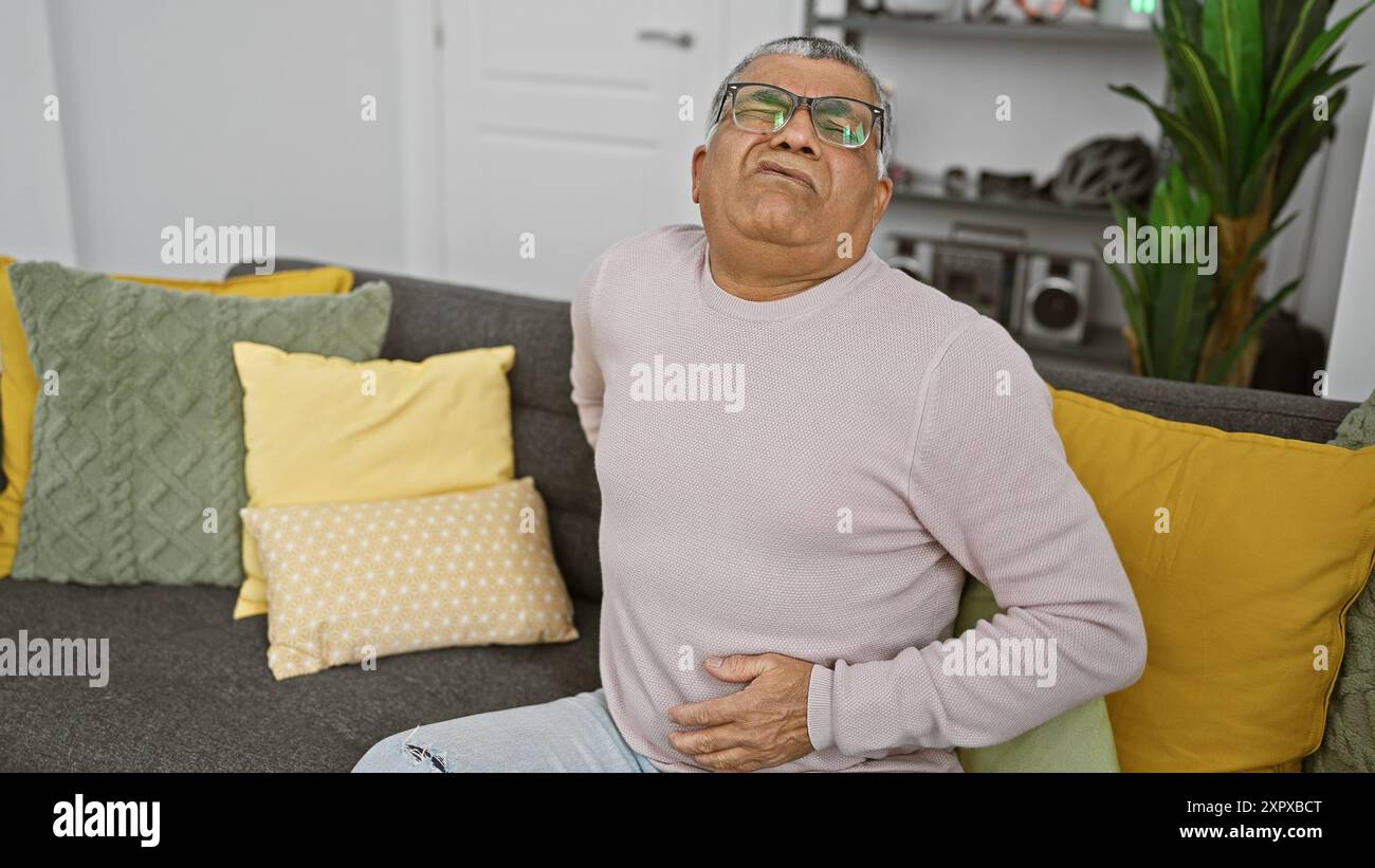 Middle-aged man expressing back pain while sitting on a couch indoors ...