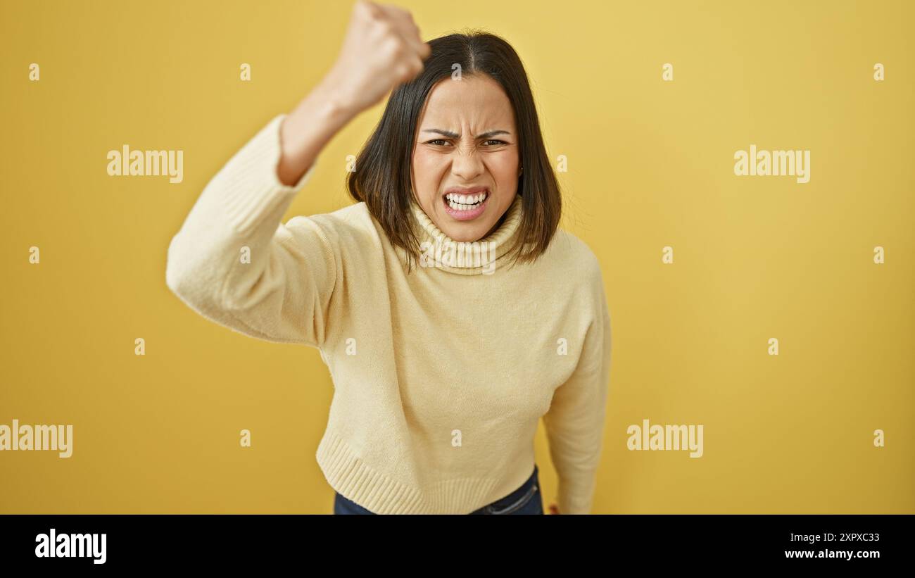 Angry hispanic woman shaking fist in frustration against a plain yellow ...