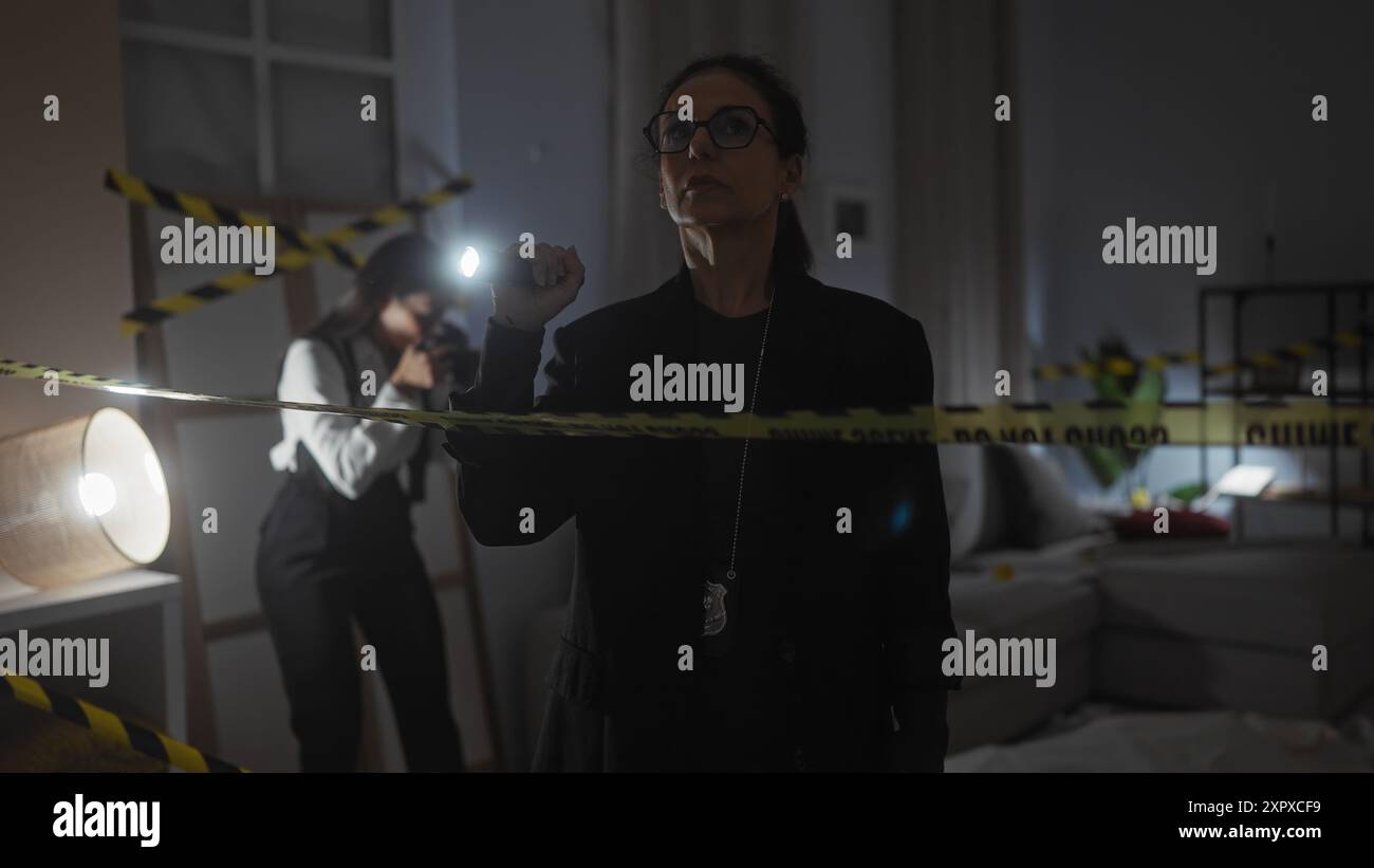 Two women investigators examine a dimly lit crime scene indoors, with ...