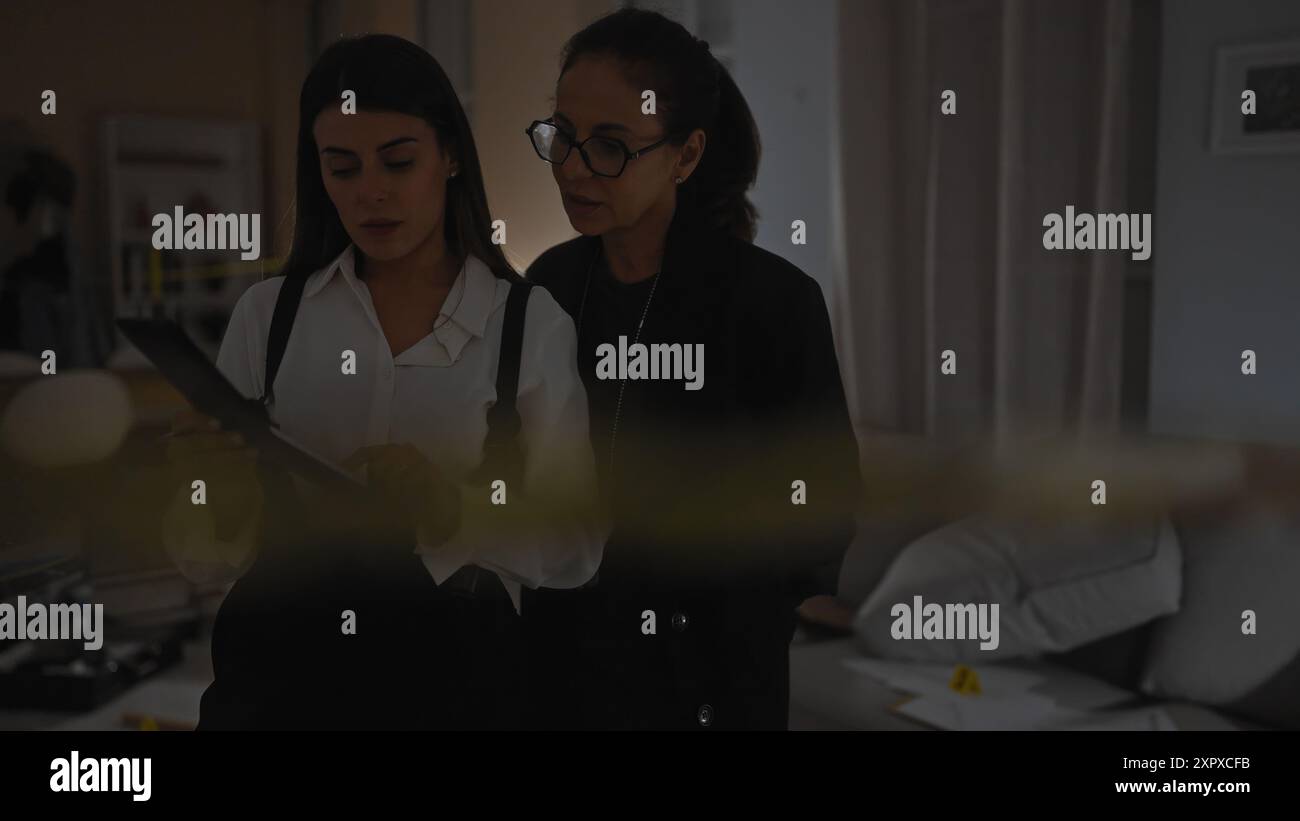 Two women investigators examine evidence in a dimly lit crime scene ...