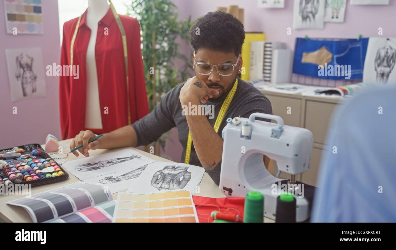 Focused african man sewing at his tailor shop, surrounded by fabric ...