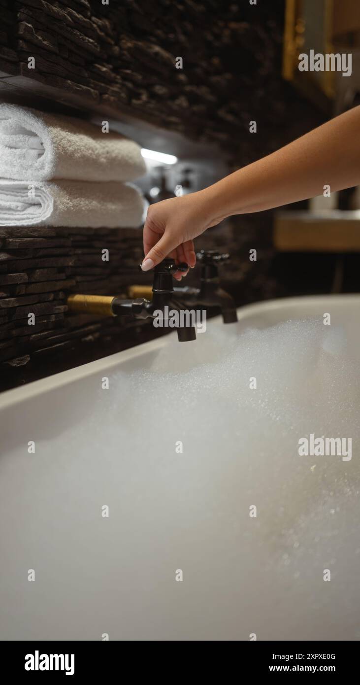 Woman preparing a bubble bath by turning on vintage faucet near a stack ...