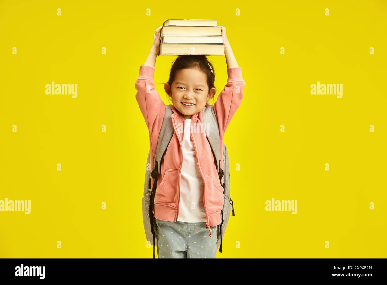 Cute chinese schoolgirl holding books on head over yellow isolated ...