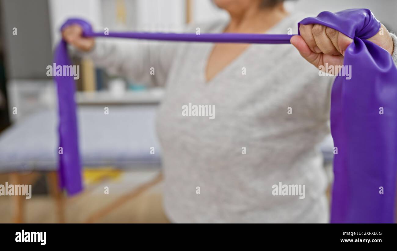 A mature woman exercises with a purple band in a therapy room ...