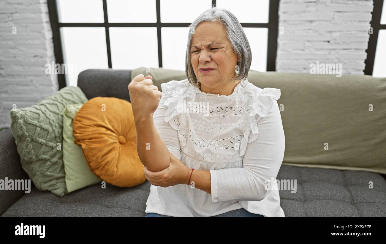 A senior woman feeling pain in her elbow while sitting on a couch at ...