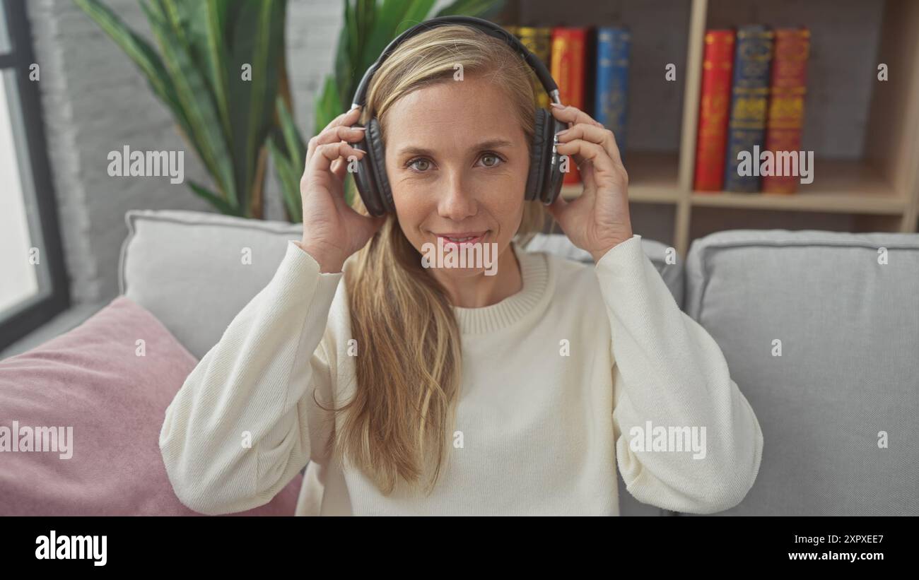 A relaxed blonde woman enjoys music with headphones on a sofa ...