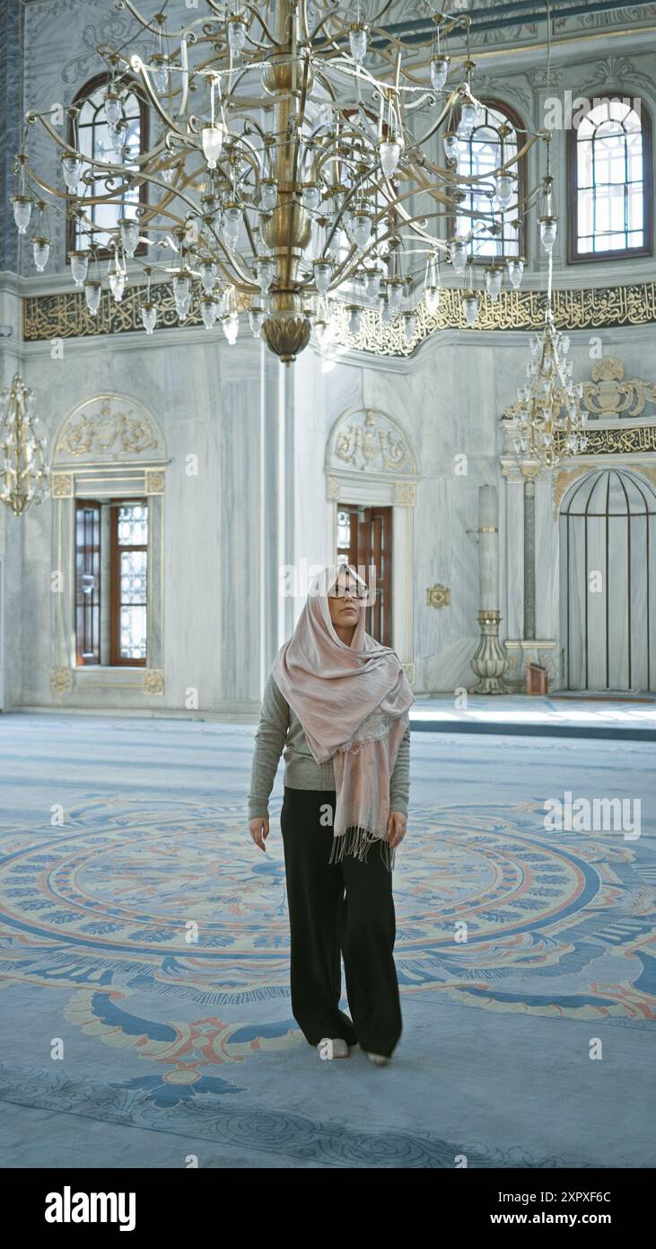 A contemplative woman wearing a hijab stands inside an ornate mosque in ...