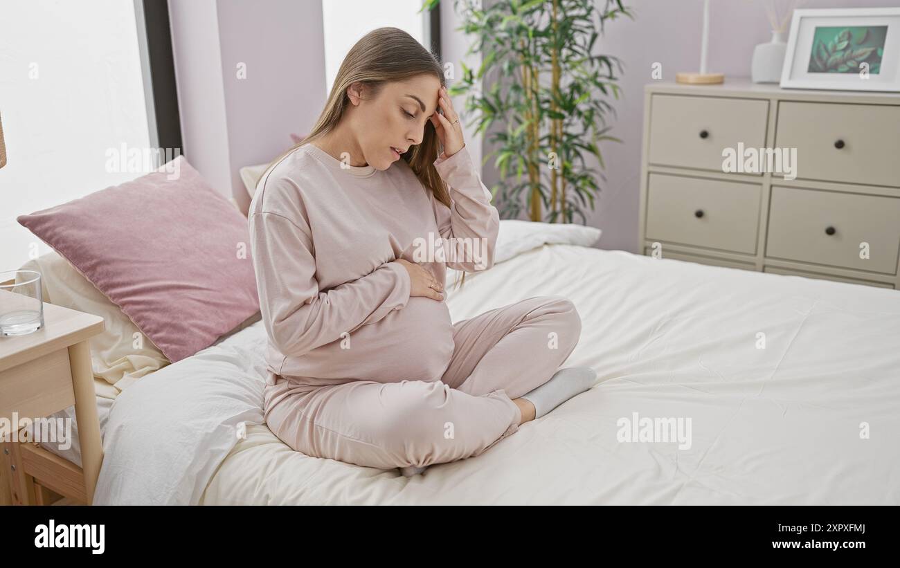 A contemplative pregnant young hispanic woman sits on a bed indoors ...