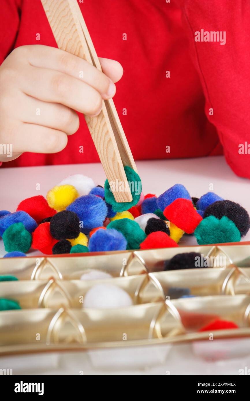 Preschooler playing with small colorful pompoms and wooden tongs ...