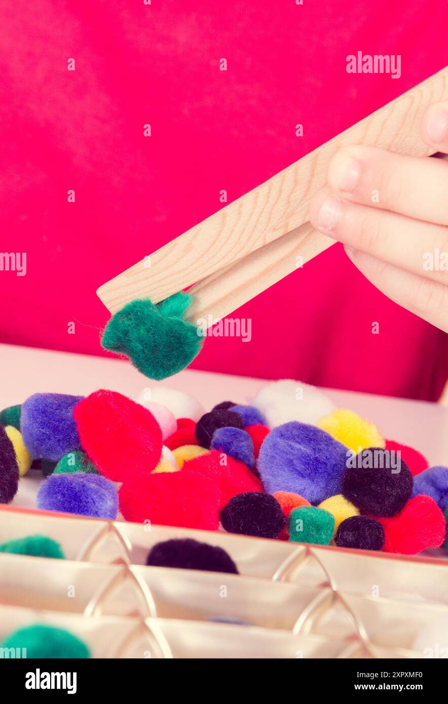 Preschooler playing with small fluffy colorful pompoms and wooden tongs ...