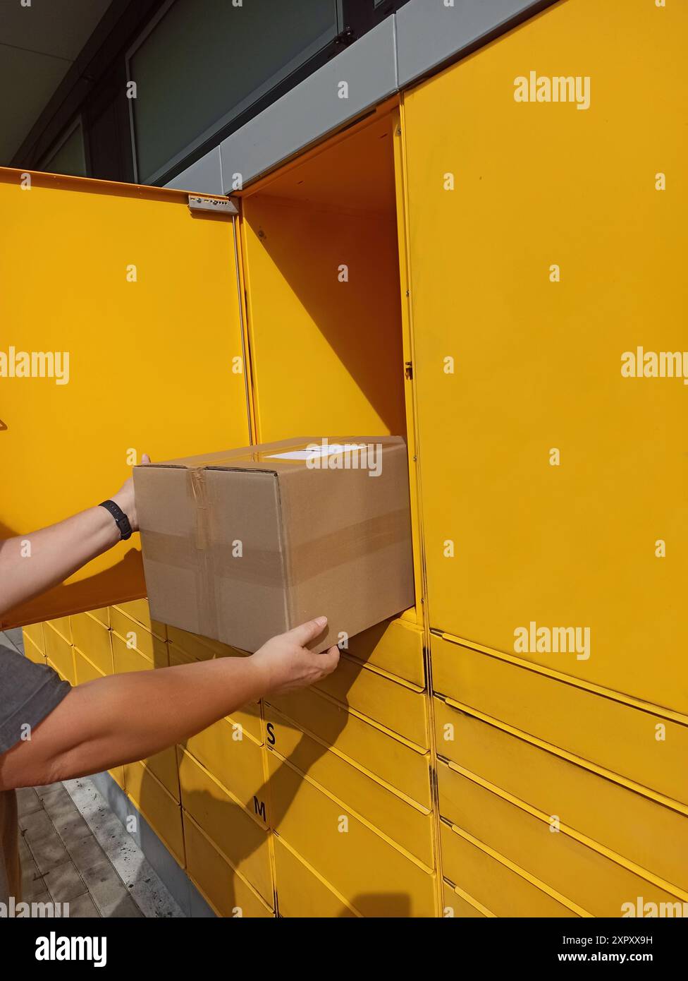a woman takes a package from a parcel station whose compartment is open ...
