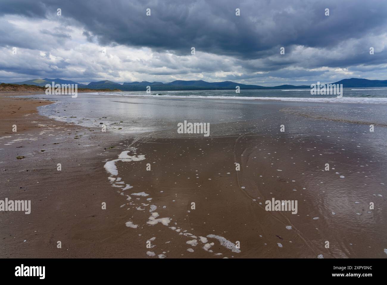 Dark grey clouds roll across Llanddwyn bay as the incoming tide washes ...