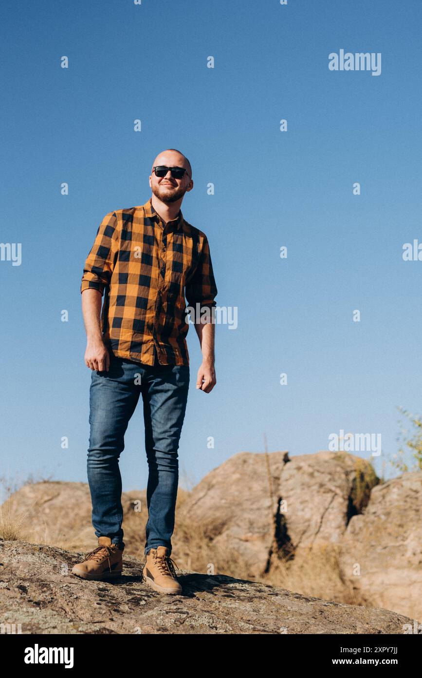 bald guy with a beard in jeans warm shirt and trekking shoes on granite ...