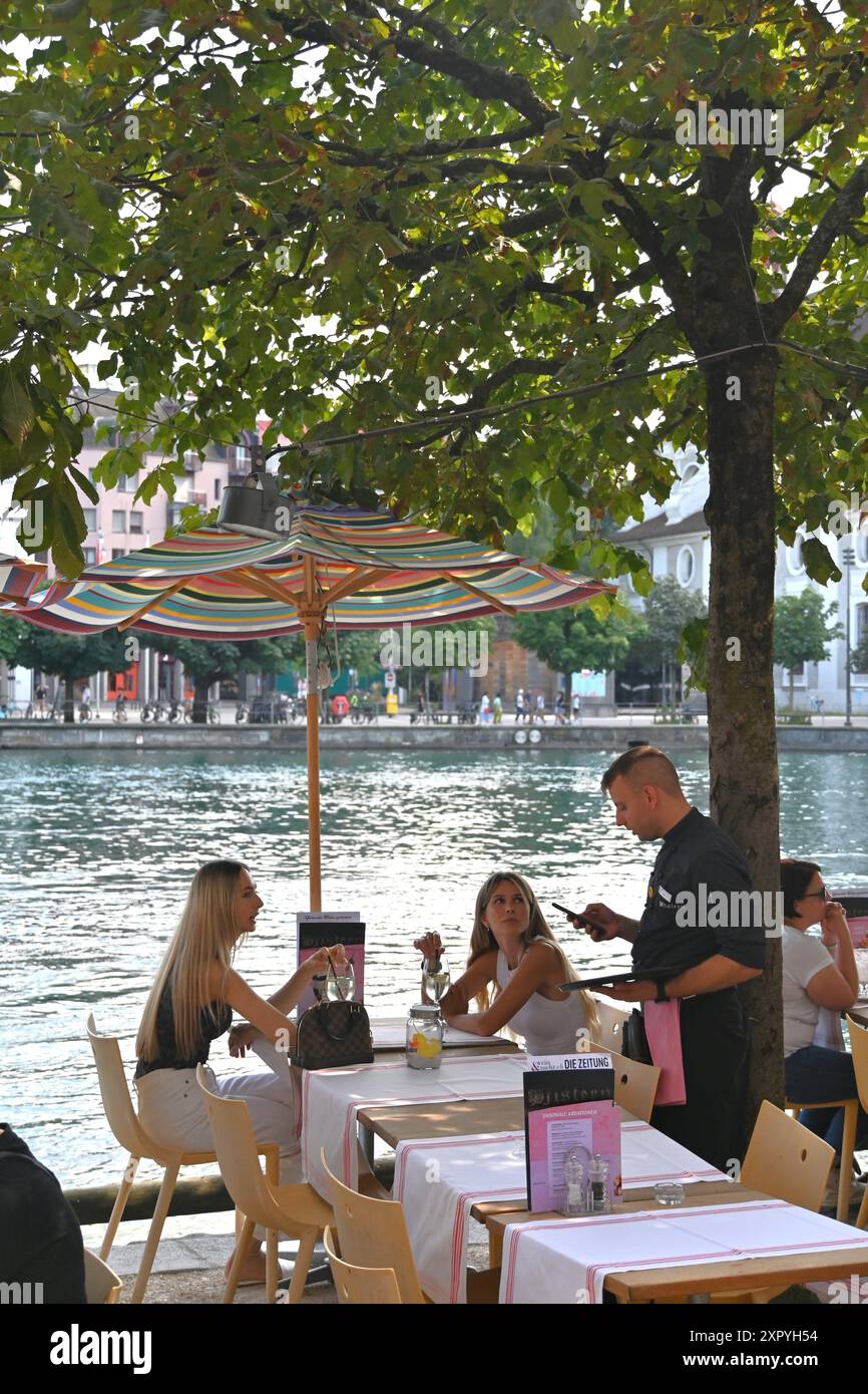 Two female tourists sitting outdoor in a bar facing river Reuss ...