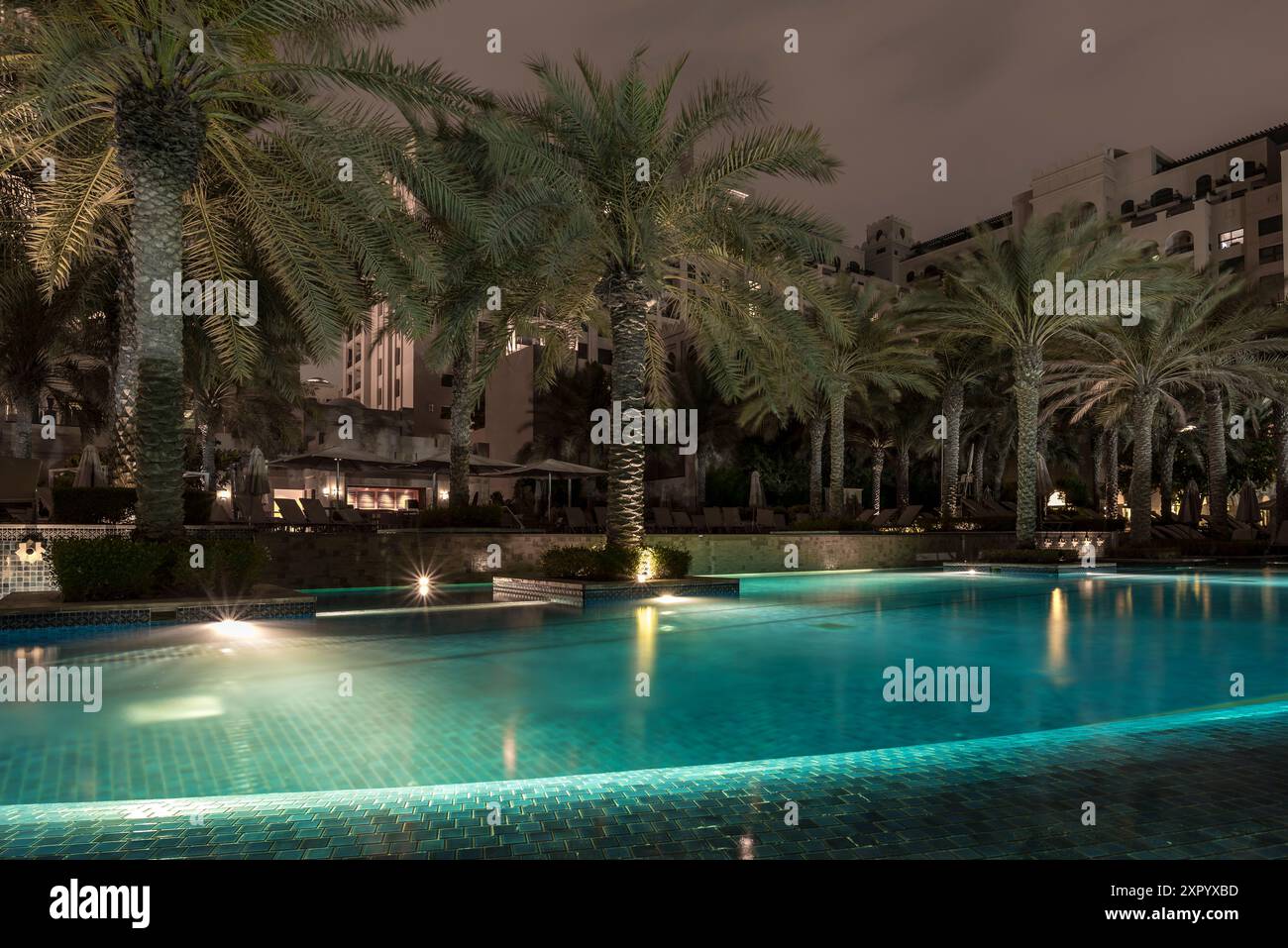 A big swimming pool, in a luxury resort, at night. The pool is ...
