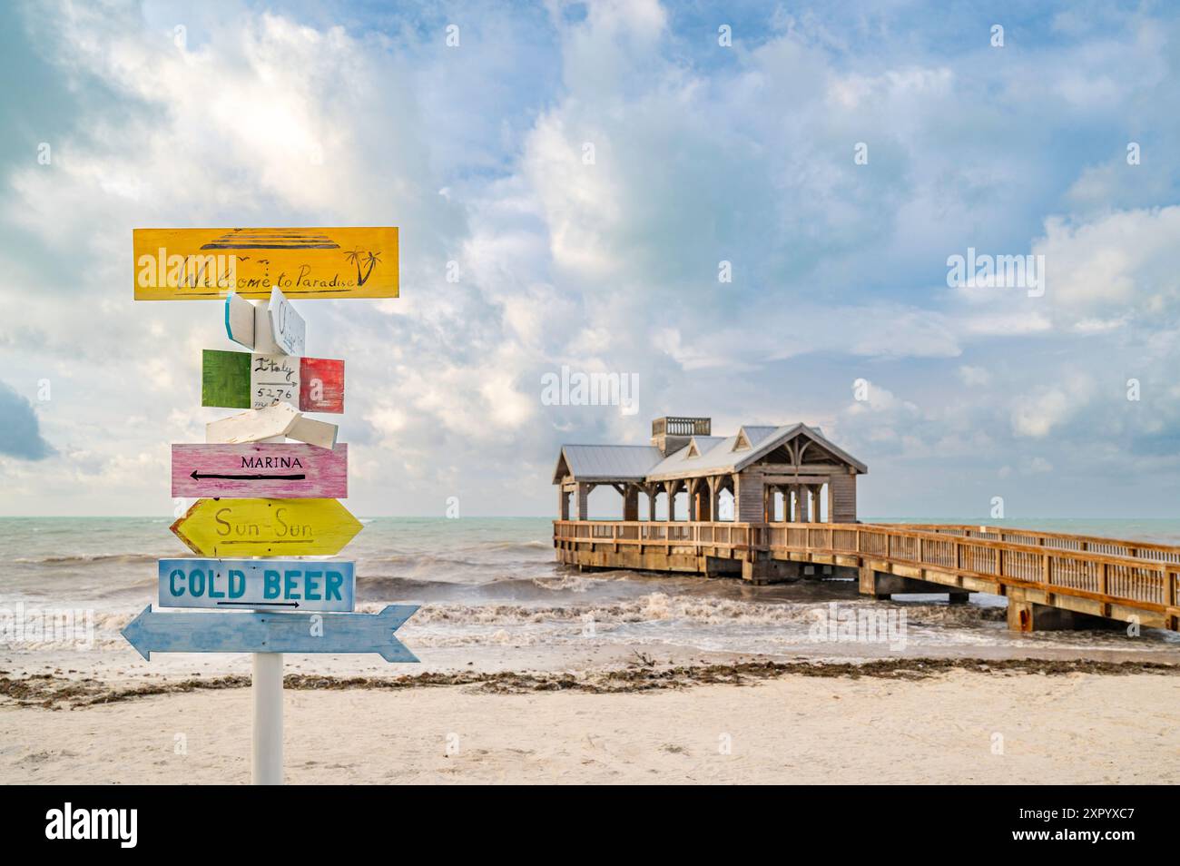 A colourful, wooden signpost, on a beach, with a wooden jetty in the ...
