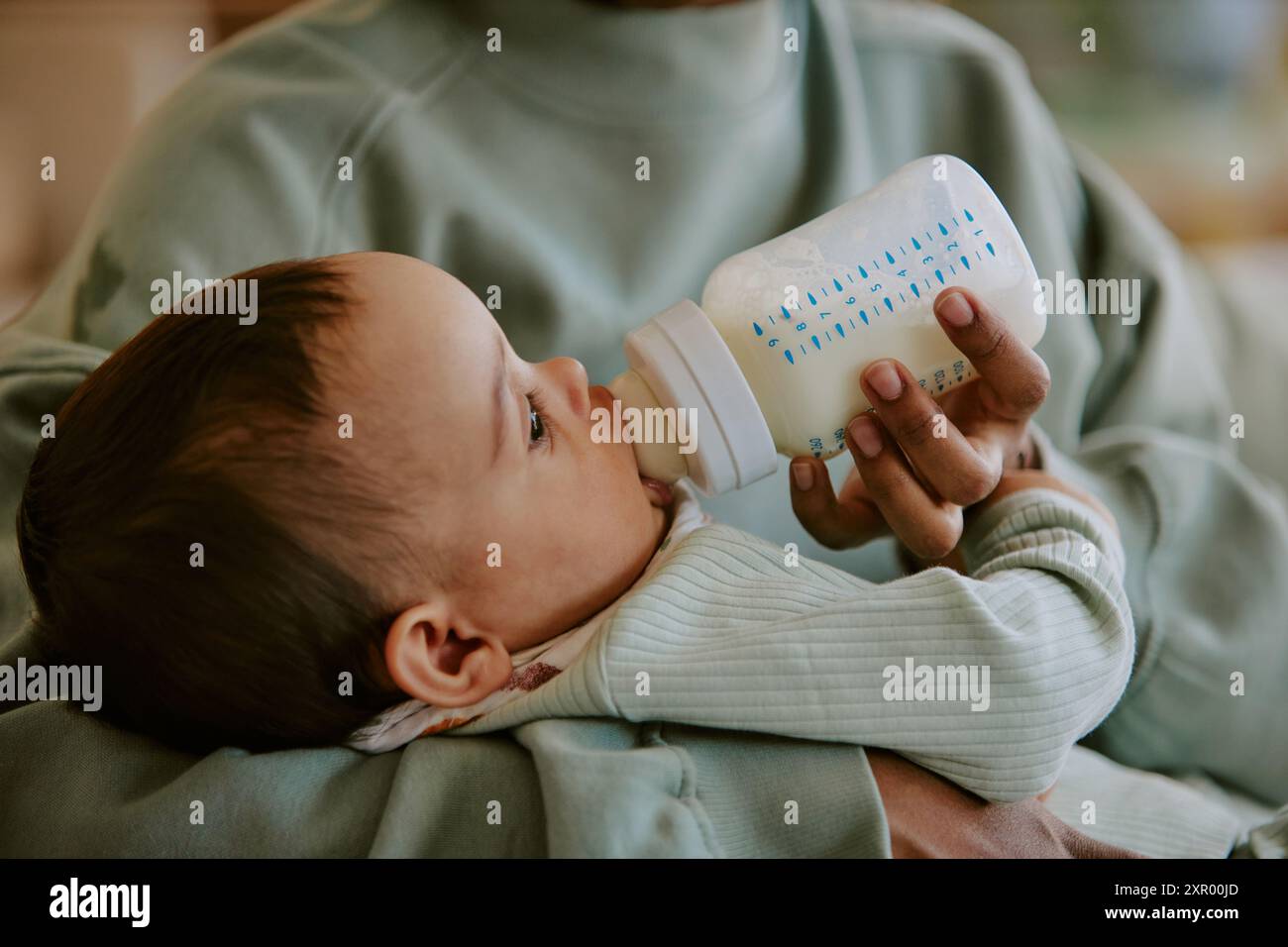 Medium close up of baby boy eating formula while his mother helping him ...