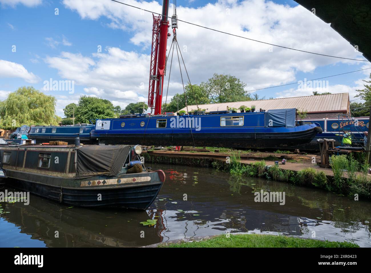 Old narrowboat being lifted by a crane out of the canal and into a boat ...
