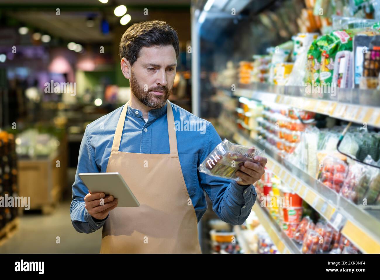 Grocery store worker holding tablet checking product on shelf in ...