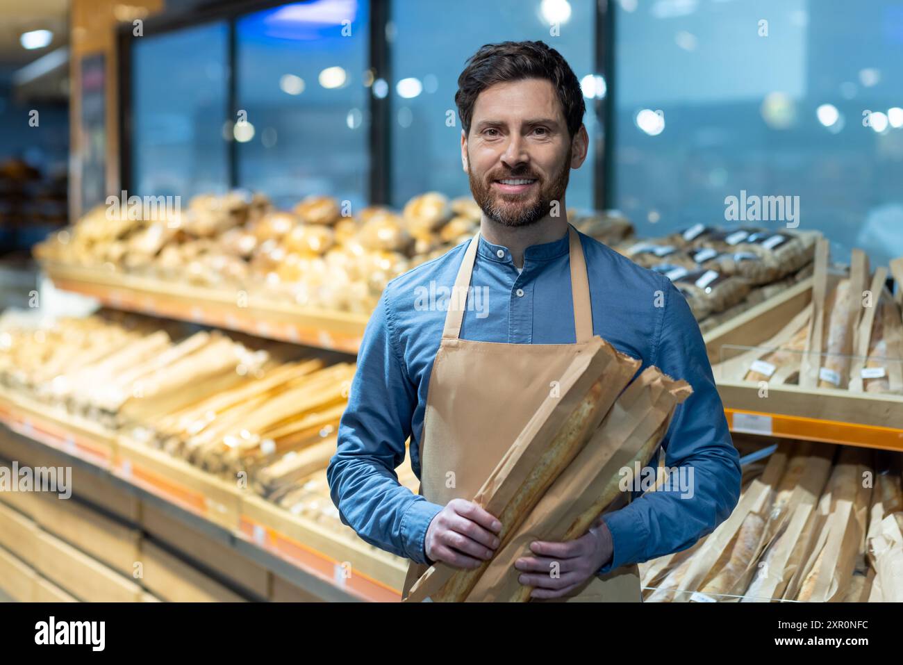 Bakery employee smiling while holding fresh baguettes. Bread section in ...