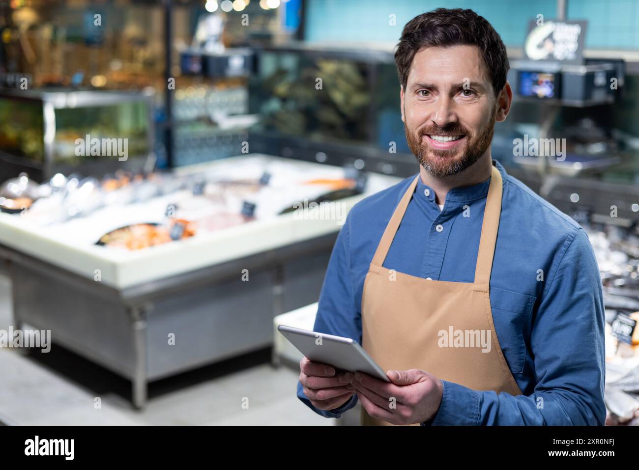 Smiling fishmonger wearing apron holding tablet in modern seafood ...