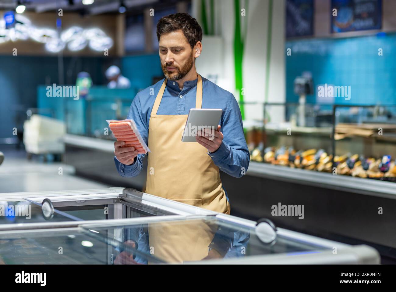 Supermarket employee wearing apron using tablet checking stock in ...