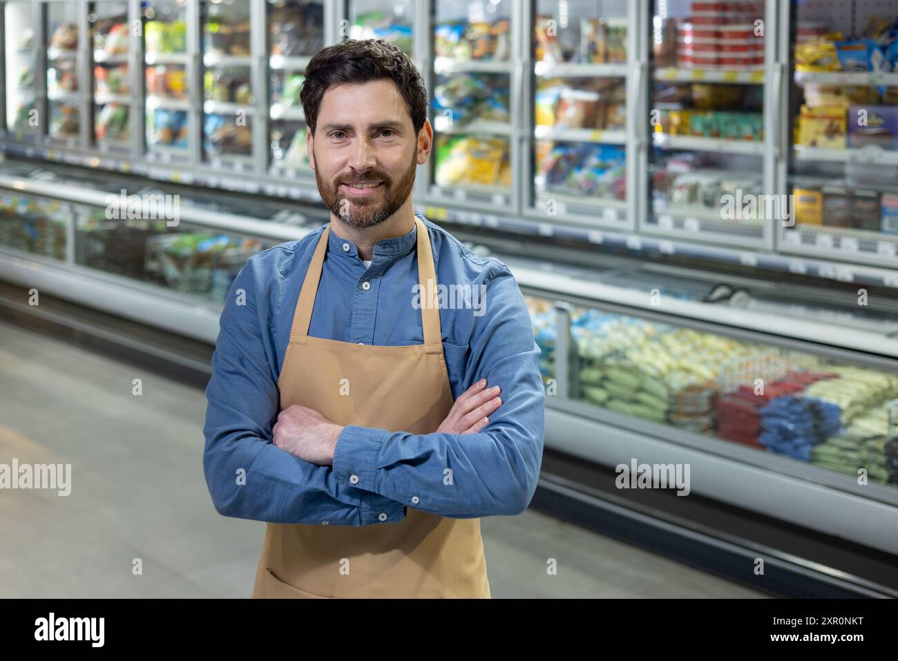 Supermarket worker standing confidently with arms crossed in front of ...