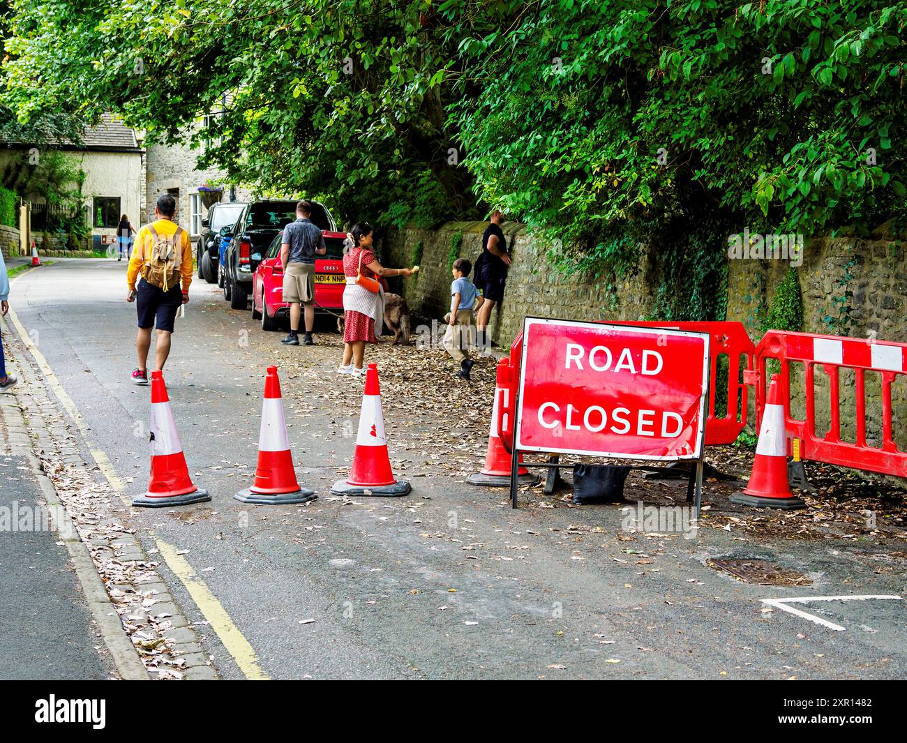 Group of people gather near a road closed sign and barriers, diverting ...