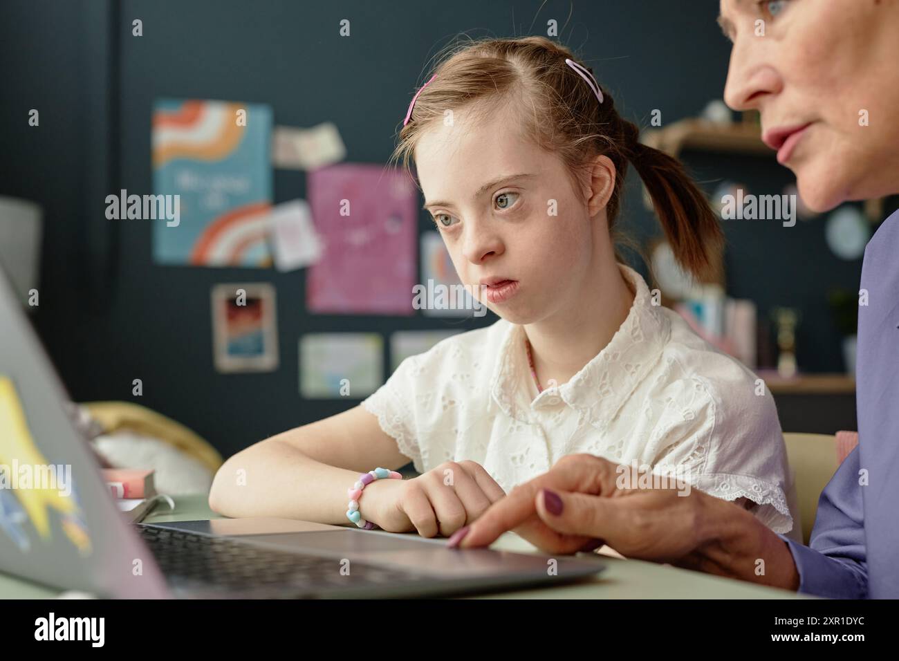 Girl with Down Syndrome engaging in home learning on laptop with adult ...