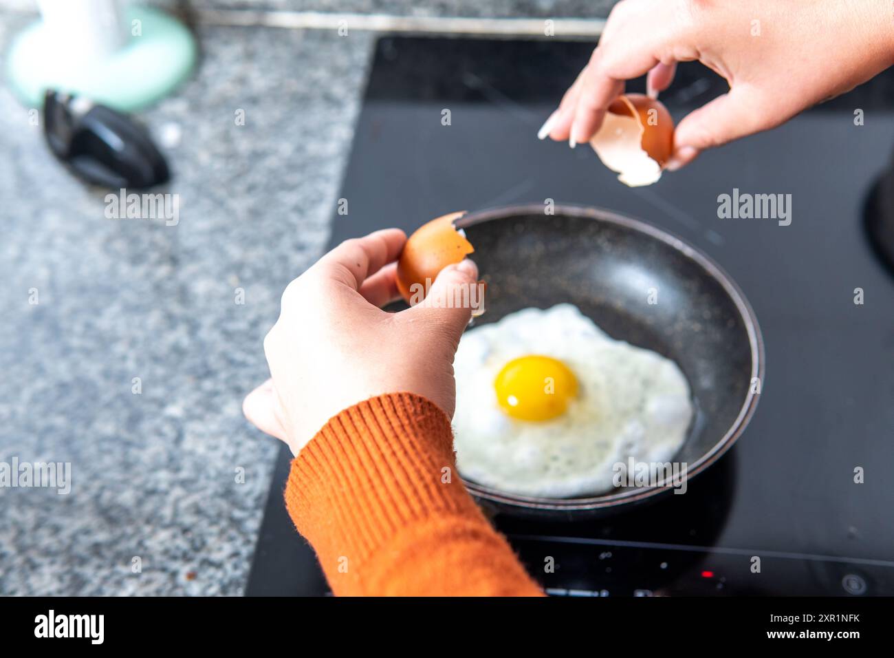 Overhead shot of woman's hands placing an egg on a frying pan on an ...