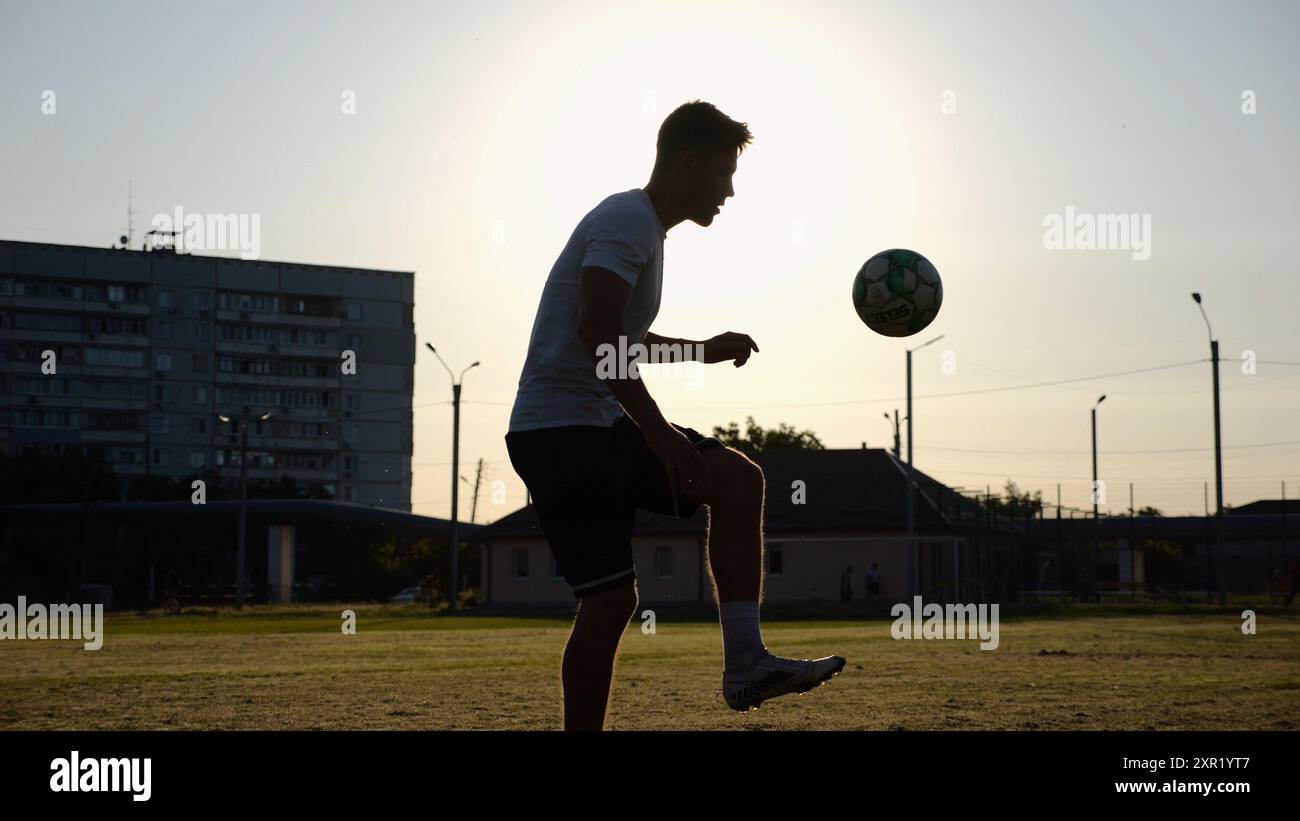 Professional footballer juggling soccer ball on stadium at sunset ...