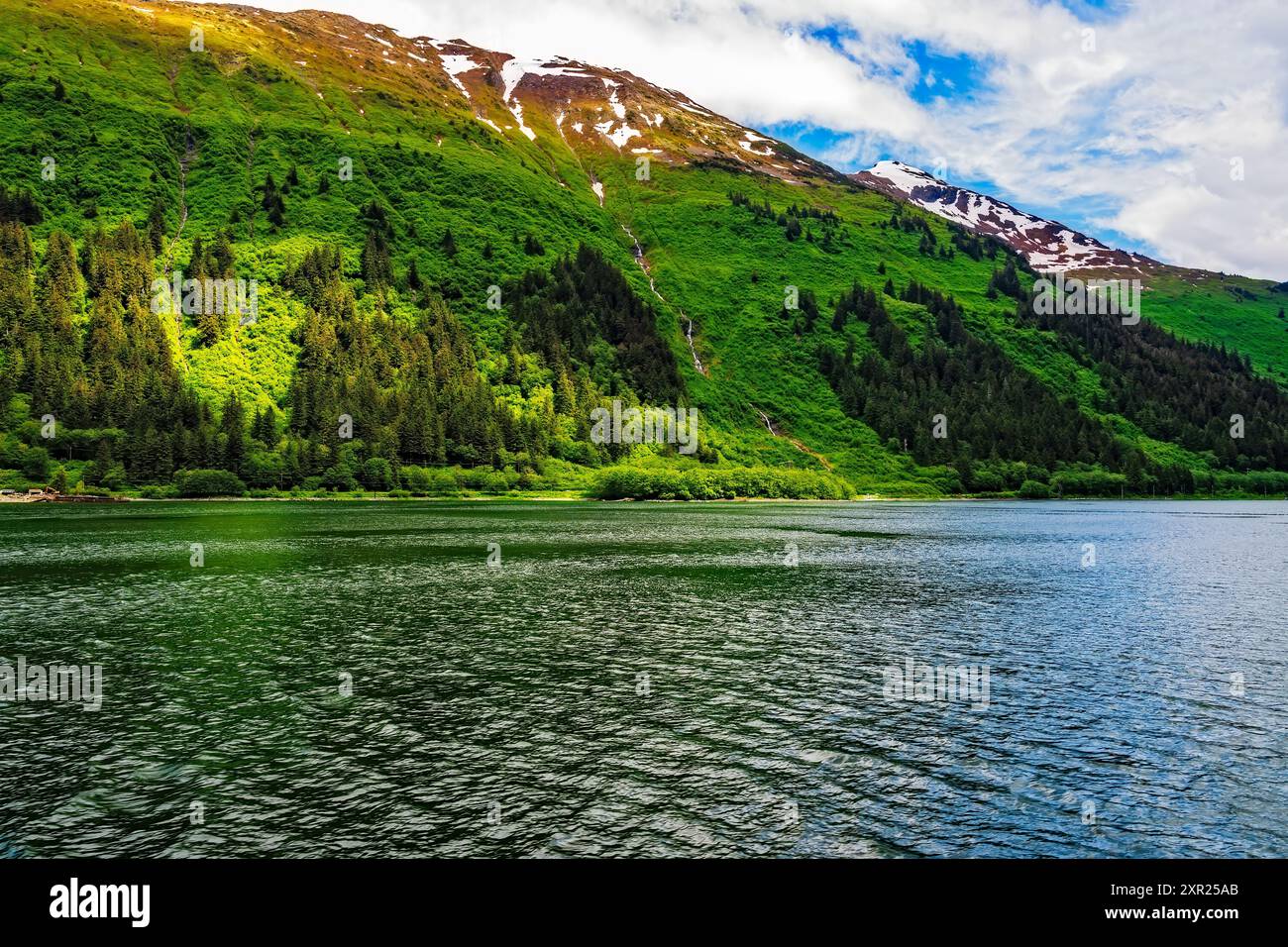 The ocean meets the shore with tall mountains covered in trees and ...