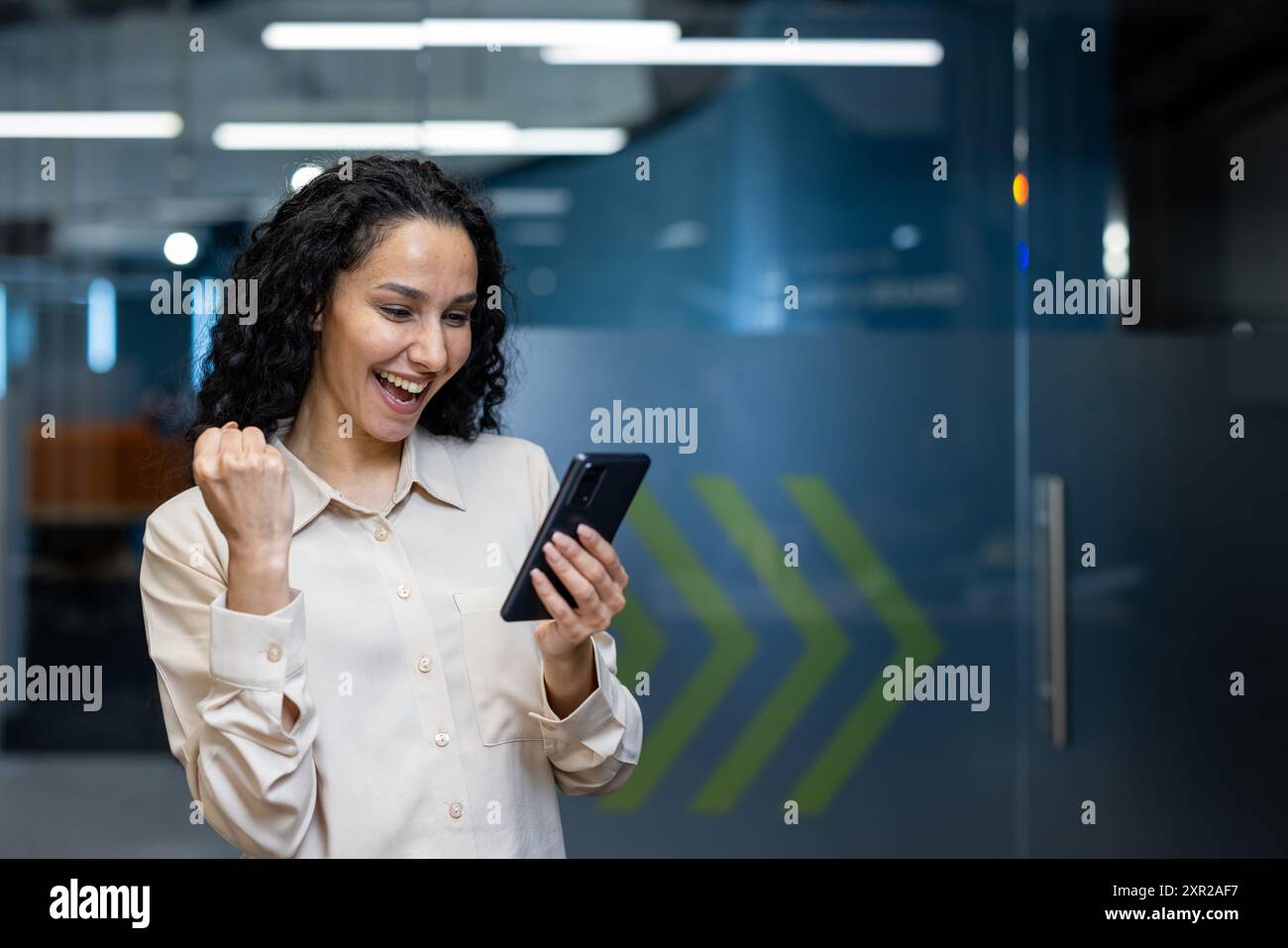 Cheerful woman celebrating success while using smartphone in office ...
