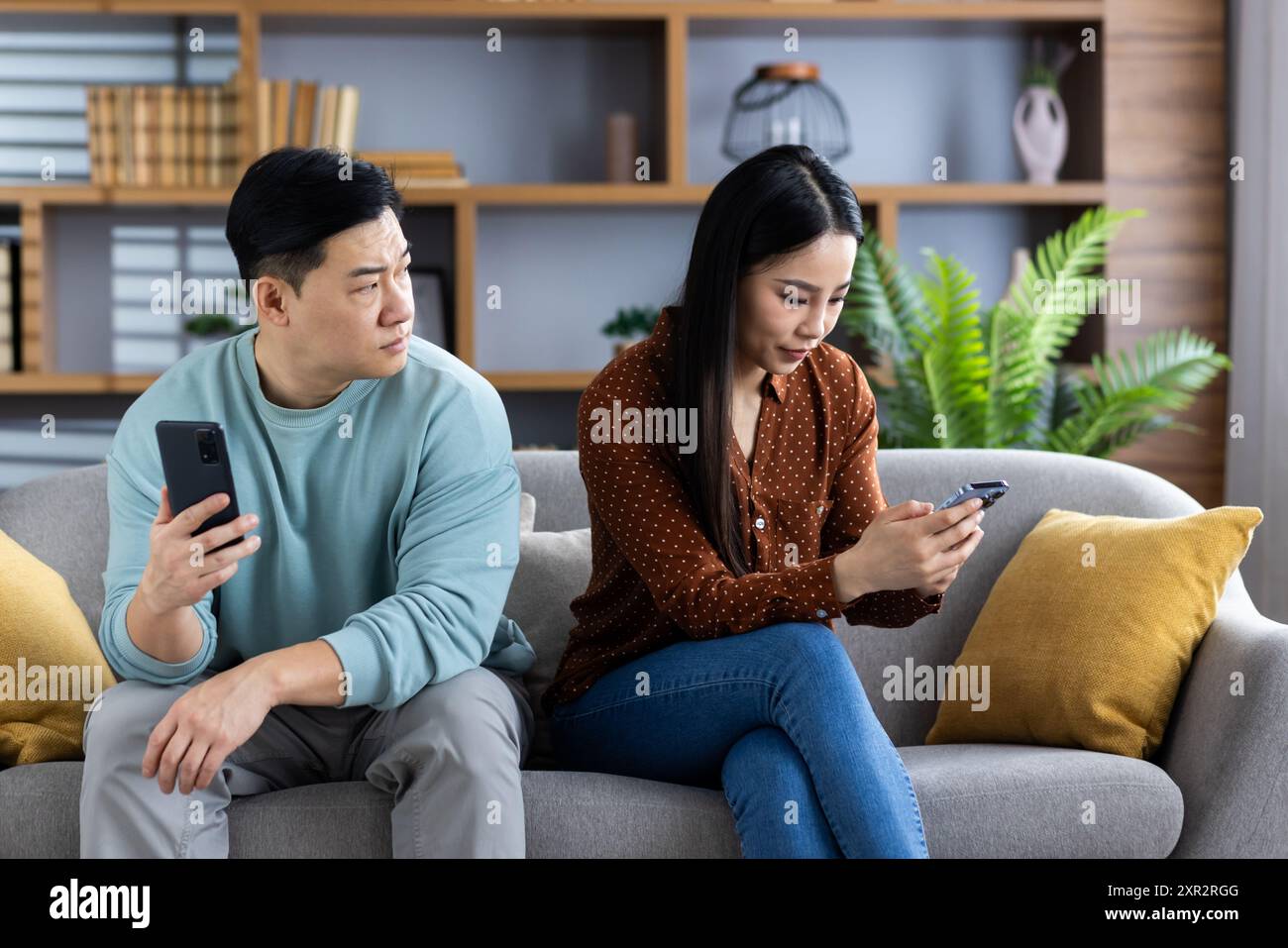 Asian couple sitting on couch both using smartphones. Depicts ...