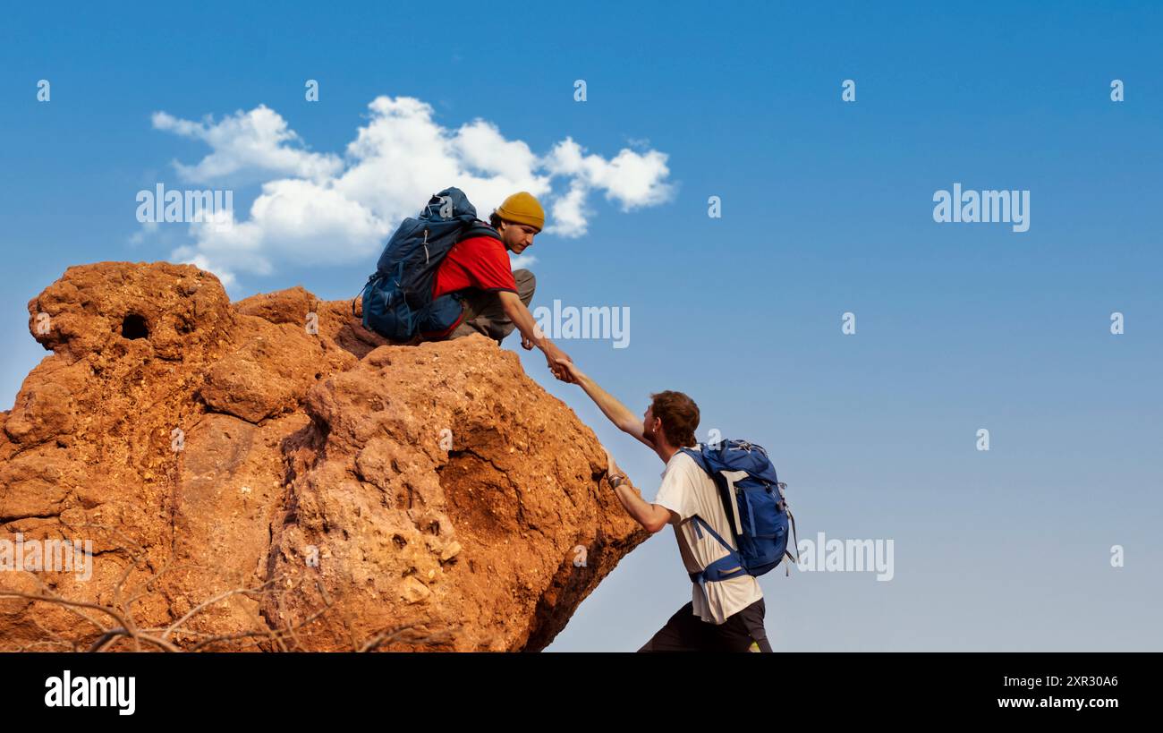 Two hikers climbing up mountain cliff and one of them giving helping ...