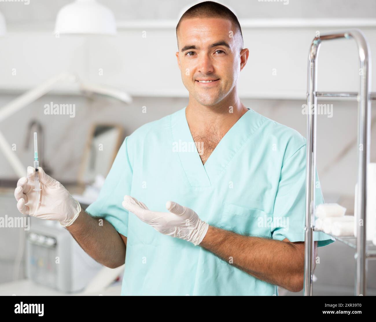 Positive man doctor posing in doctor cabinet holding syringe in his ...