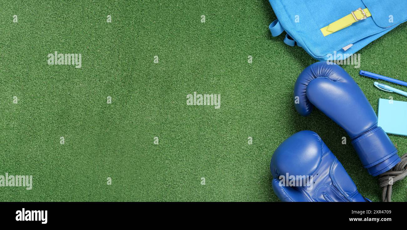Backpack with boxing gloves and school stationery on green grass ...