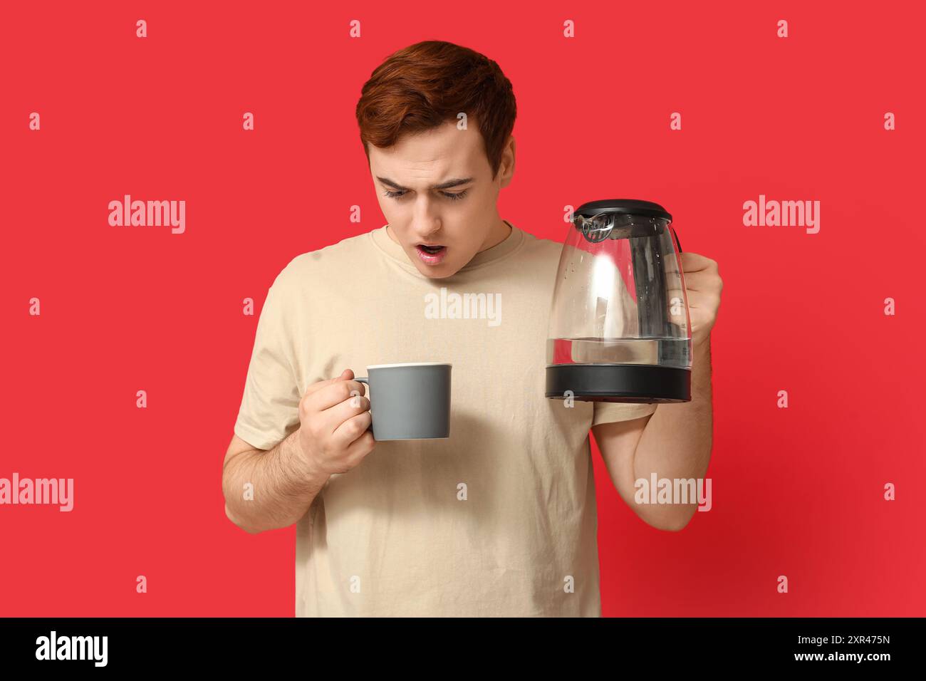 Shocked young man with modern electric kettle and mug on red background ...