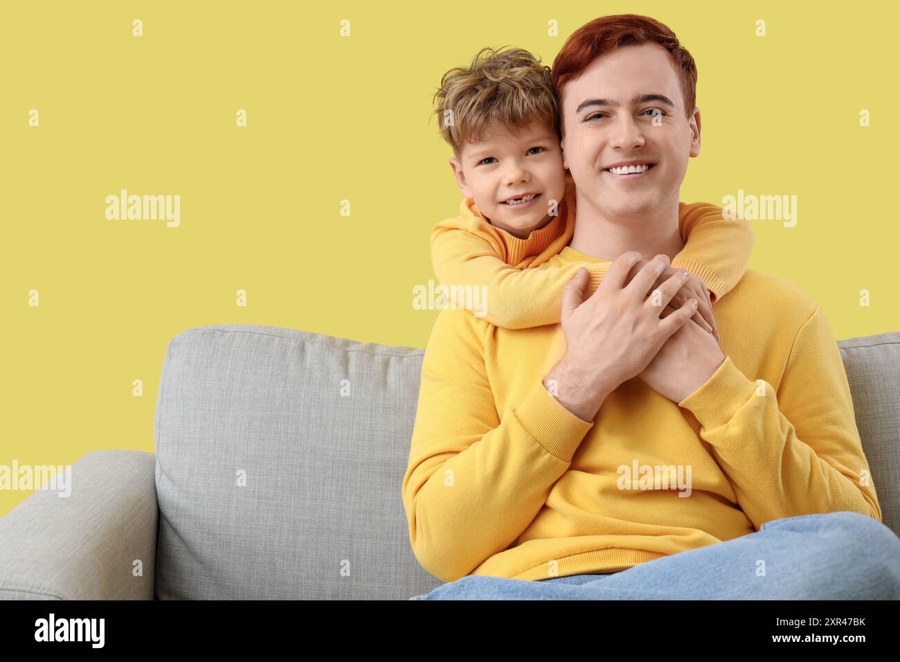 Little boy hugging his father on sofa against yellow background Stock ...
