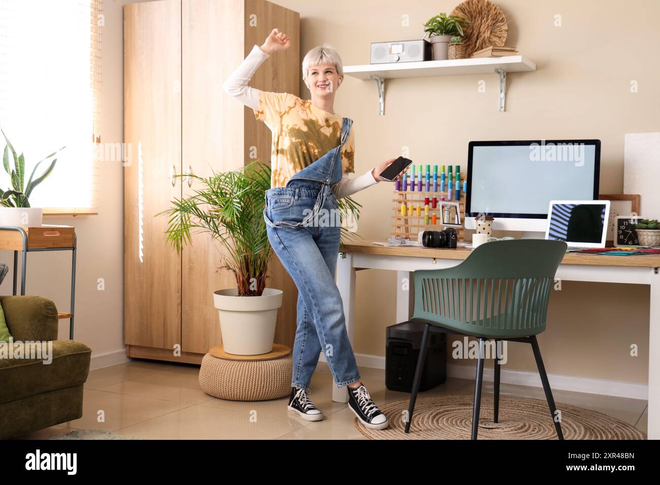 Young woman holding mobile phone near workplace with modern computer in ...