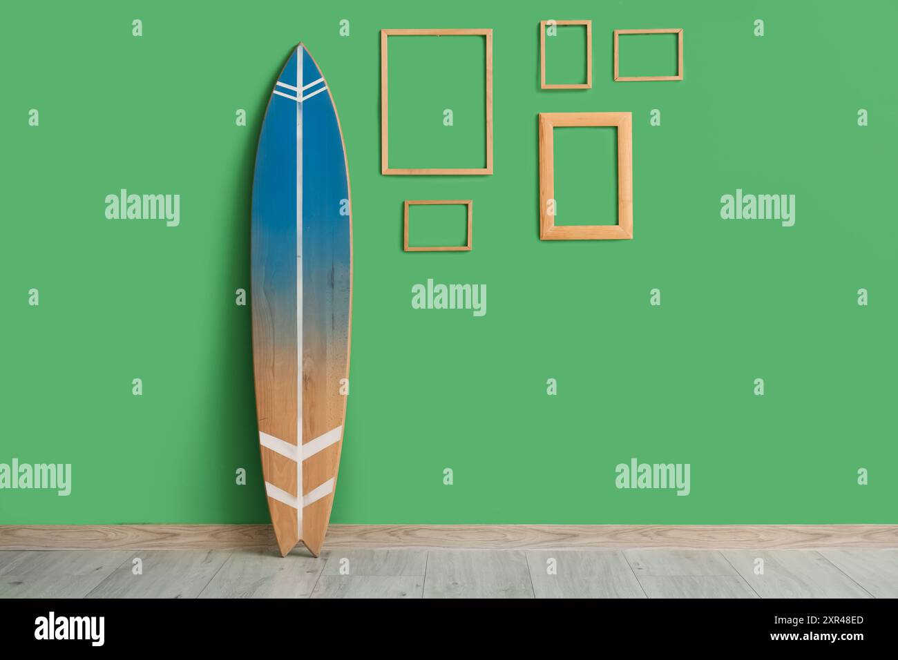 Wooden surfboard and frames on green wall in room Stock Photo - Alamy
