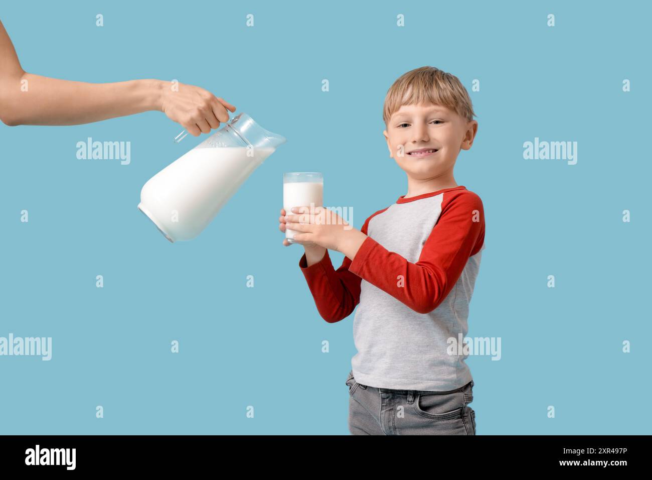 Female hand pouring milk in glass for little boy on blue background ...