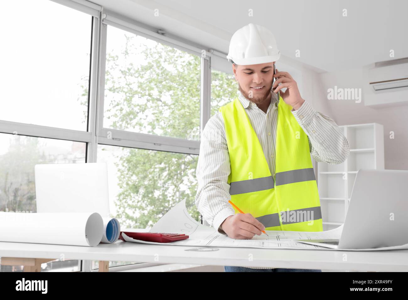 Male contractor with house plan talking by mobile phone in room Stock ...